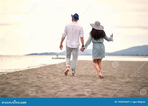 Caucasian Young Adult Couple In Love Walking Barefoot On Sandy Beach