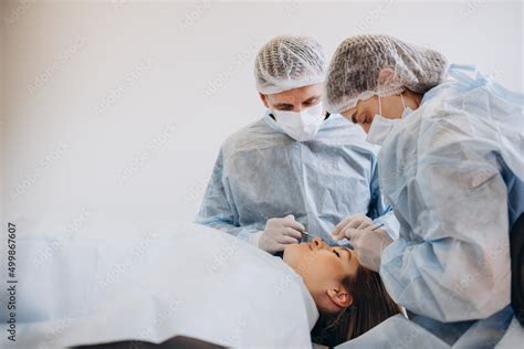 Surgeon And His Assistant Performing Cosmetic Surgery On Nose In