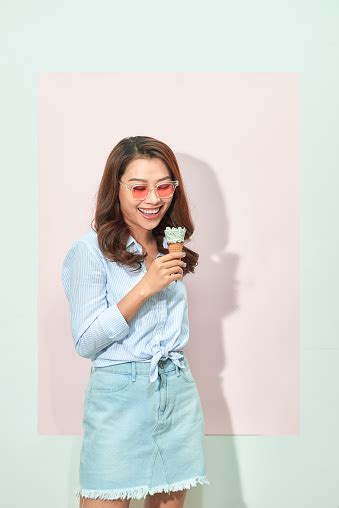 행복 한 즐거운 젊은 아시아 여자를 가진 웃는 얼굴이 카메라에 보인다 맛 있는 아이스크림을 보유 관광 복장에 밝은 분홍색 배경에