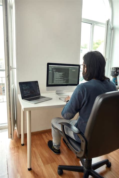 Back View Of Male Web Developer Writing Code While Sitting At His