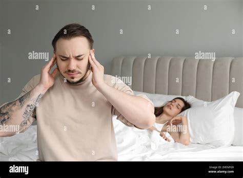 Bedtime Irritated Man Covering Ears Near His Snoring Wife In Bed At
