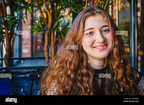 A Girl With Long Brown Wavy Hair Smiles Showing Her Teeth Sitting At A