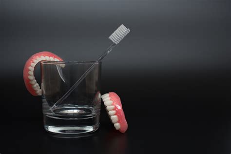 턱의 전체 이동식 플라스틱 틀니 두 개의 아크릴 의치 칫솔으로 치과 진료를 할 수 있습니다 어두운 배경에 치아와 칫솔 치과 보철