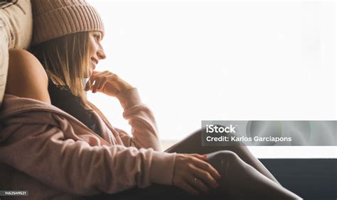 모자를 쓰고 창문 옆에 있는 옆모습의 여자가 웃고 있다 행복과 휴식의 개념 자연 채광 30 34세에 대한 스톡 사진 및 기타 이미지 30 34세 가정 생활 개념