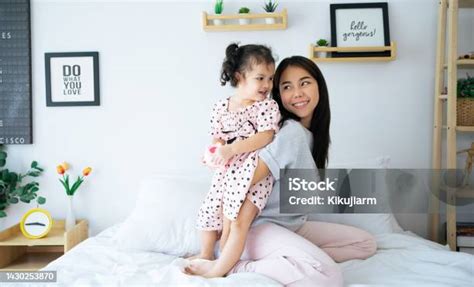 행복한 아시아 가족입니다 미혼모와 아이 딸은 창문에서 햇빛이 들어오는 집안의 침대에서 함께 놀고 있는 세 살의 딸입니다 어버이