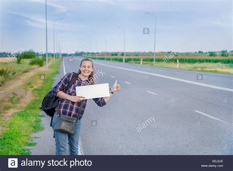 Smiling Woman Hitchhiker On The Road Is Holding A Blank Board Concept