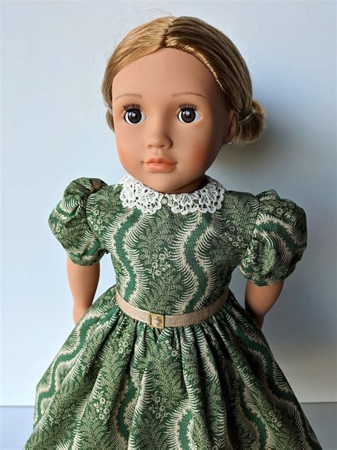 The Doll Is Wearing A Green Dress With White Lace On Its Neckline