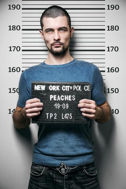 Premium Photo Mug Shot Of Young Man Holding Placard Against Wall With