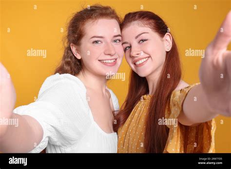 Beautiful Young Redhead Sisters Taking Selfie On Orange Background