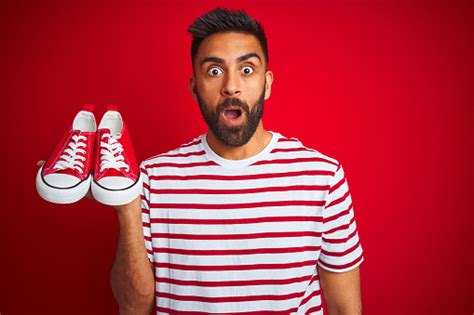 젊은 아랍 인도 히스패닉 남자 들고 스포츠 캐주얼 운동화 위에 고립 된 빨간 배경 에 무서워 충격으로 충격으로 깜짝 얼굴 두려움과 두려움 표현흥분 경외감에 대한 스톡 사진