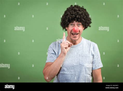 Man With Black Wig And Red Clown Nose Posing In Front Of Green