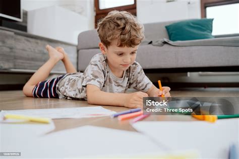 한 학령기 소년이 거실 바닥에 누워 있고 흰색 종이에 컬러 마커가 있는 그림을 그립니다 소년은 집에서 오후 자유 시간을 보내고있다 가정의 방에 대한 스톡 사진 및 기타