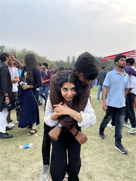 Two People Hugging Each Other In The Middle Of A Group Of People Standing On Grass
