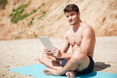 Het Glimlachen Mens Zitting En Het Gebruiken Van Tablet Op Het Strand