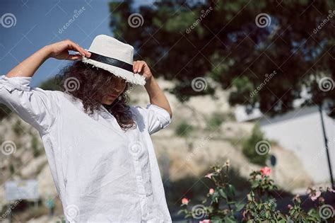 Woman Adjusting Hat In A Sunny Outdoor Setting With Relaxed Summer