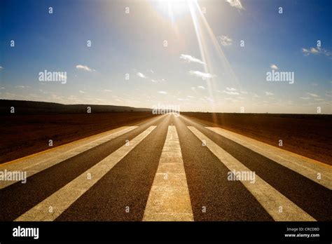 Wide Angle Shot Of Long Straight Road With Runway Markings And Sun In