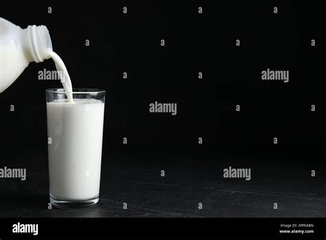 Pouring Milk From Gallon Bottle Into Glass On Black Table Space For