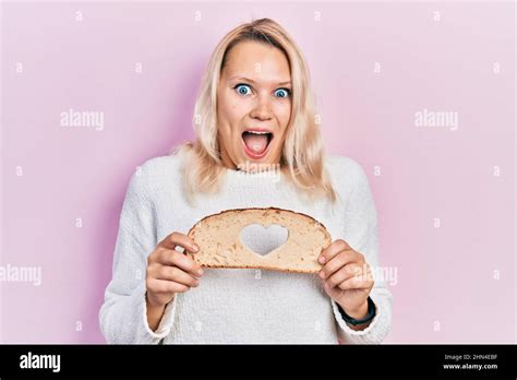 Beautiful Caucasian Blonde Woman Holding Bread Loaf With Heart Shape Celebrating Crazy And