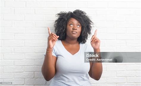 젊은 아프리카계 미국인 플러스 크기 여자 흰 벽돌에 깜짝 놀라게 하 고 놀 보고 하 고 손가락으로 가리키는 벽 하 고 무기를