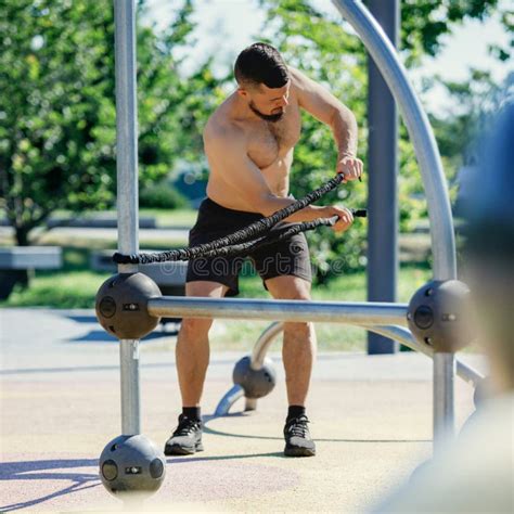 Bearded Man Performing Resistance Band Exercises Shirtless In Black