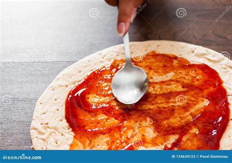 Hand Woman Cook With Spoon Smears Tomato Sauce On Dough Making Italian