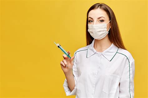 의료복을 입은 젊은 여성의 초상화와 의료 주사기를 손에 들고 보호 마스크를 쓰고 복사 공간이 있는 노란색 배경에서 고립되어
