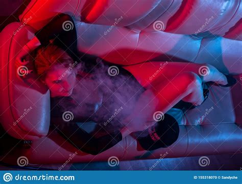 Redhead Woman In Black Bodysuit Sitting On A Sofa And Smokes Hookah