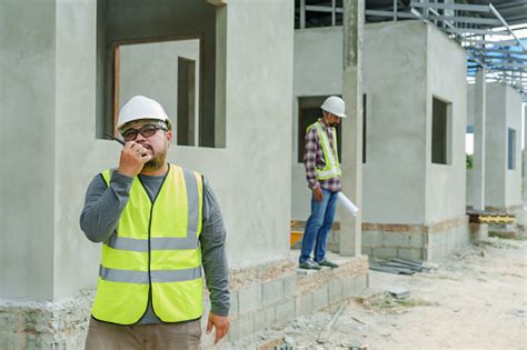 건설 안전 조끼를 입은 남성이 전화 통화를 하고 있고 안전모와 청사진을 쓴 또 다른 남성이 미완성 건물 계단에 서 있다 건축가와 엔지니어는 주택 건설을 감독합니다 35 39