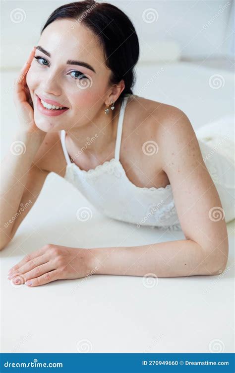 Beautiful Brunette Woman In A White Dress Lies In A Bright Room Stock
