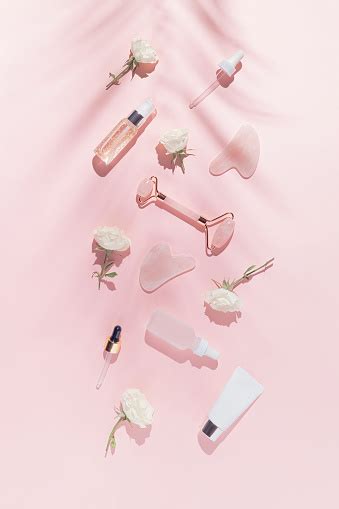 홈 스킨 케어용 페이셜 키트 얼굴 롤러 구아 샤 마사지 흰색 장미 싹과 그림자와 핑크 파스텔 햇볕에 빛나는 배경에 화장품 세럼병