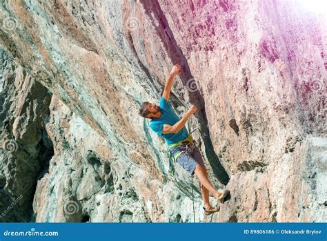 Montanhista Masculino Maduro Que Faz O Movimento Arriscado Na Rocha Sun Que Brilha Foto De Stock