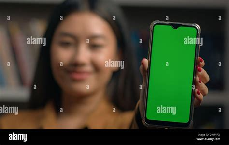 Smiling asian woman girl holding smartphone showing new application close-up green empty screen ...