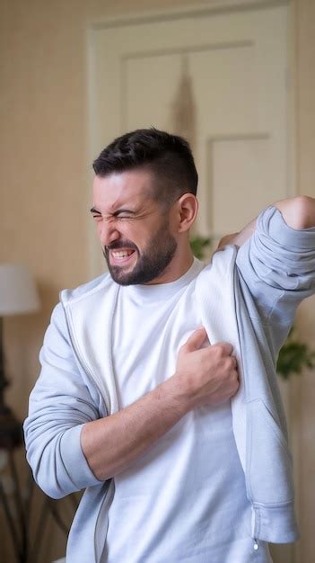 Man In Sweat Smelling His Armpit Standing In White Tshirt And Grimacing