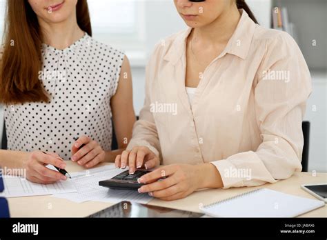 Two Female Accountants Counting On Calculator Income For Tax Form Completion Hands Closeup