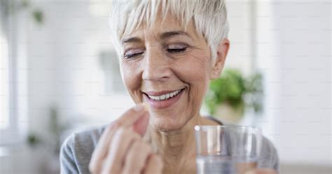 웃고 있는 행복한 건강한 중년 50대 여성이 물 한 잔을 들고 건강 보조 비타민 알약을 복용하고 있다 노화 방지 아름다움을 위한 노인 종합 비타민 항산화제 사진