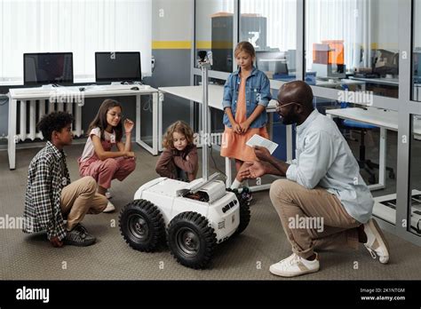 Young Teacher Of Robotics With Tablet Making Presentation Of Crawler To Group Of Intercultural