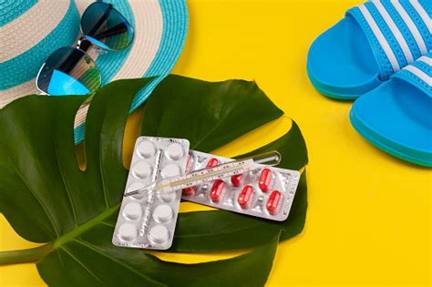 물집 팩 파란색 모자 파란색 플립 플롭 선글라스 노란색 배경에 몬스터 잎에 온도계 흰색과 빨간색 알약에 상단보기 해변 휴가 바다 투어 따뜻한 화창한 여름의 개념 적응 여행