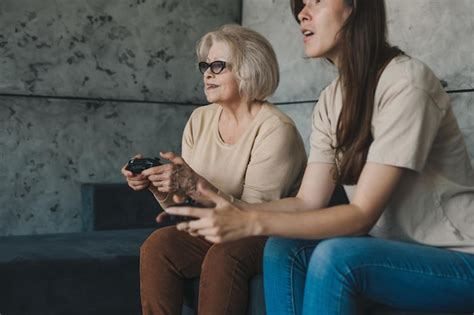 Velha avó jovem mãe jogando videogame em casa sentada no sofá usando joysticks para design de