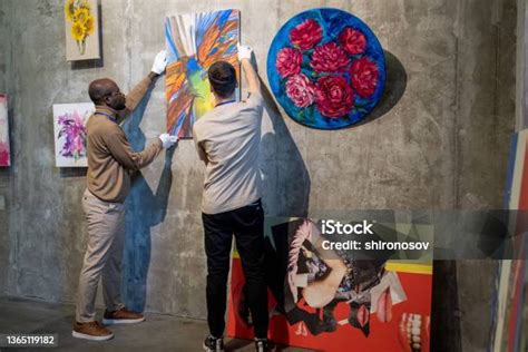 벽에 매달려 그림을 매달려 예술 갤러리의 두 젊은 남성 노동자 전시회에 대한 스톡 사진 및 기타 이미지 전시회 준비 직원
