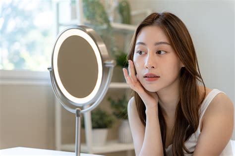 거울 앞에 앉아 있는 아름다운 아시아 여자 크림과 화장을 하는 건강한 여자의 얼굴 스킨 크림 주름 방지 크림 아기 얼굴 스킨