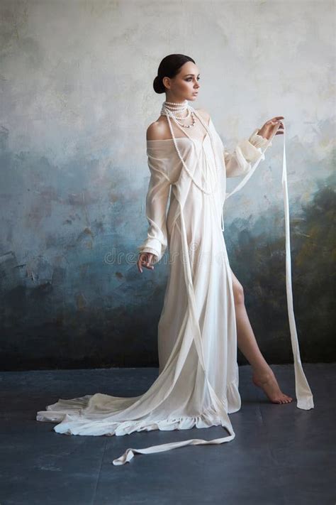 Belle Fille Mince Brune Assis Sur Le Sofa Dans Une Longue Robe Blanche Portrait Dune Femme Avec