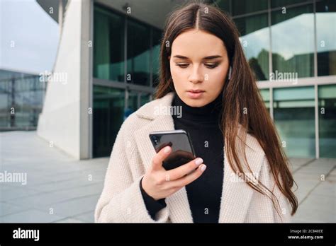 Portrait Of Beautiful Brunette Girl Intently Using Cellphone On City