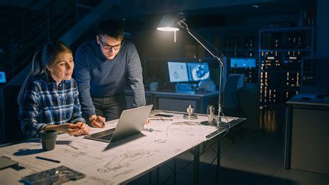 산업 공학 시설 데스크톱 컴퓨터에서 작업하는 여성 엔지니어 프로젝트 관리자가 옆에 서서 작업 및 프로젝트 세부 사항의 세부 사항을 설명합니다 엔진 프로토타입 에 늦게 작업