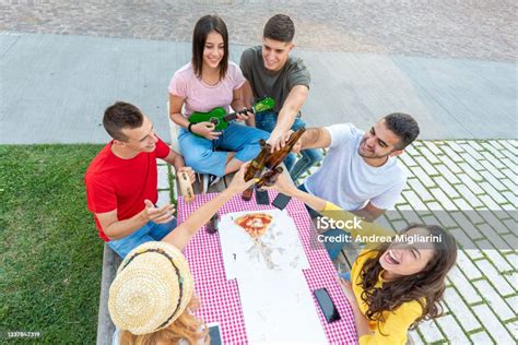 나무 테이블을 들고 노래하고 놀고 있는 친구들이 피자와 맥주 한 병을 빼앗아 긍정적인 소식을 전하고 젊은 밀레니엄 세대의 파티를