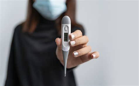 얼굴 마스크를 가진 여자 손은 흰색 배경에 고립 된 의료 온도계를 보유하고 있습니다 발열 또는 진단 자가 검진 의료 및 의료