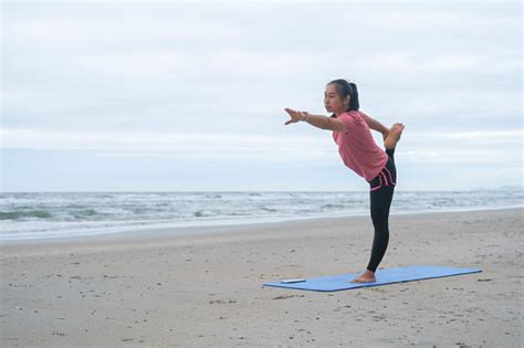 해변에서 요가를 연습하는 아시아 여성 해변의 푸른 요가 매트에서 야외에서 스트레칭을하고 요가를하는 젊은 아름다운 여성 자연에서