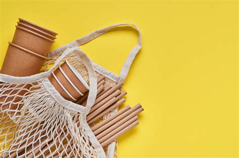종이와 옥수수 전분으로 만든 갈색 튜브 빨대 메쉬 마켓 백 및 트렌디 한 회색과 노란색 배경에 빈 종이 커피 컵을 마시는 제로