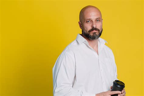 흰색 셔츠를 입은 잘생긴 진지한 중년 남성이 미소를 지으며 복사 공간이 있는 노란색 배경에 커피 한 잔을 들고 있다 노인의 초상화 40 49세에 대한 스톡 사진 및 기타