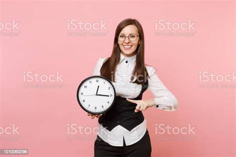 양복과 안경 알람 시계 파스텔 핑크 배경에 고립에 검지 손가락을 가리키는 성공적인 비즈니스 젊은 여자 여자 보스입니다 성과 경력 부 개념입니다 광고에 대 한 공간을 복사