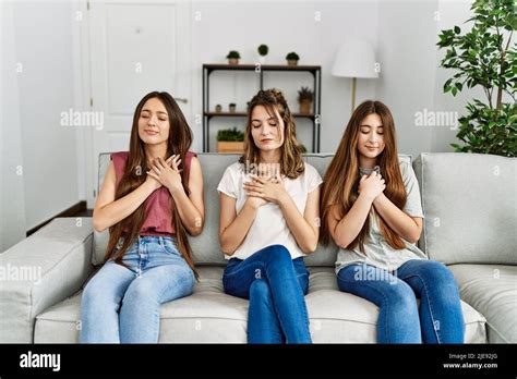 Group Of Three Hispanic Girls Sitting On The Sofa At Home Smiling With
